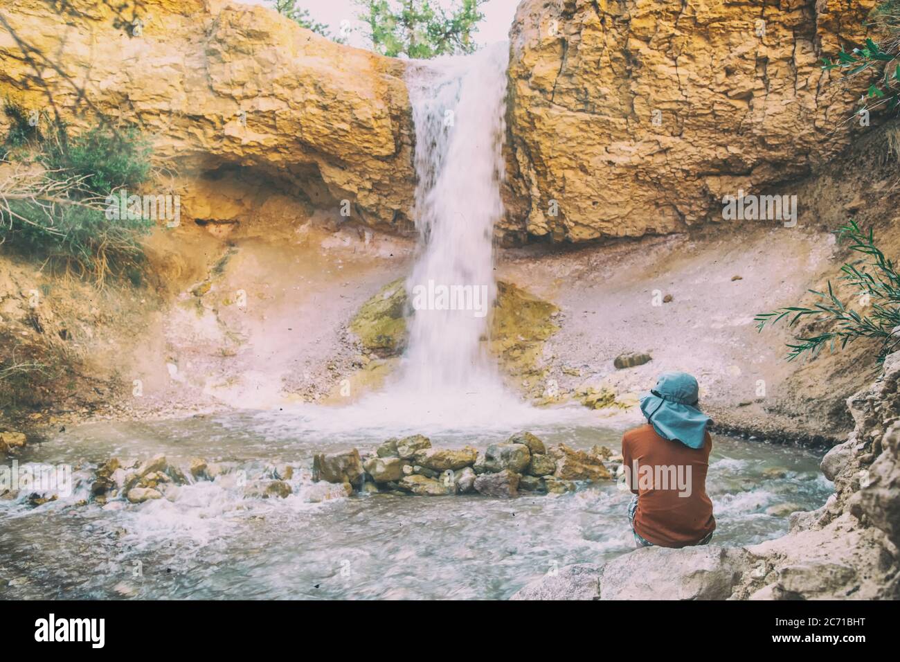 Back view of woman wearing hat looking at a natural waterfalls inside ...