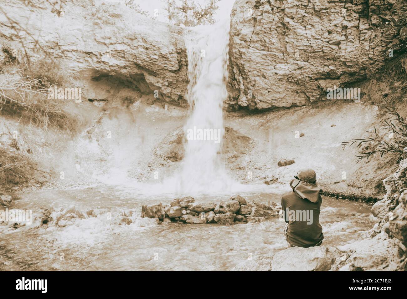 Back view of woman wearing hat looking at a natural waterfalls inside ...