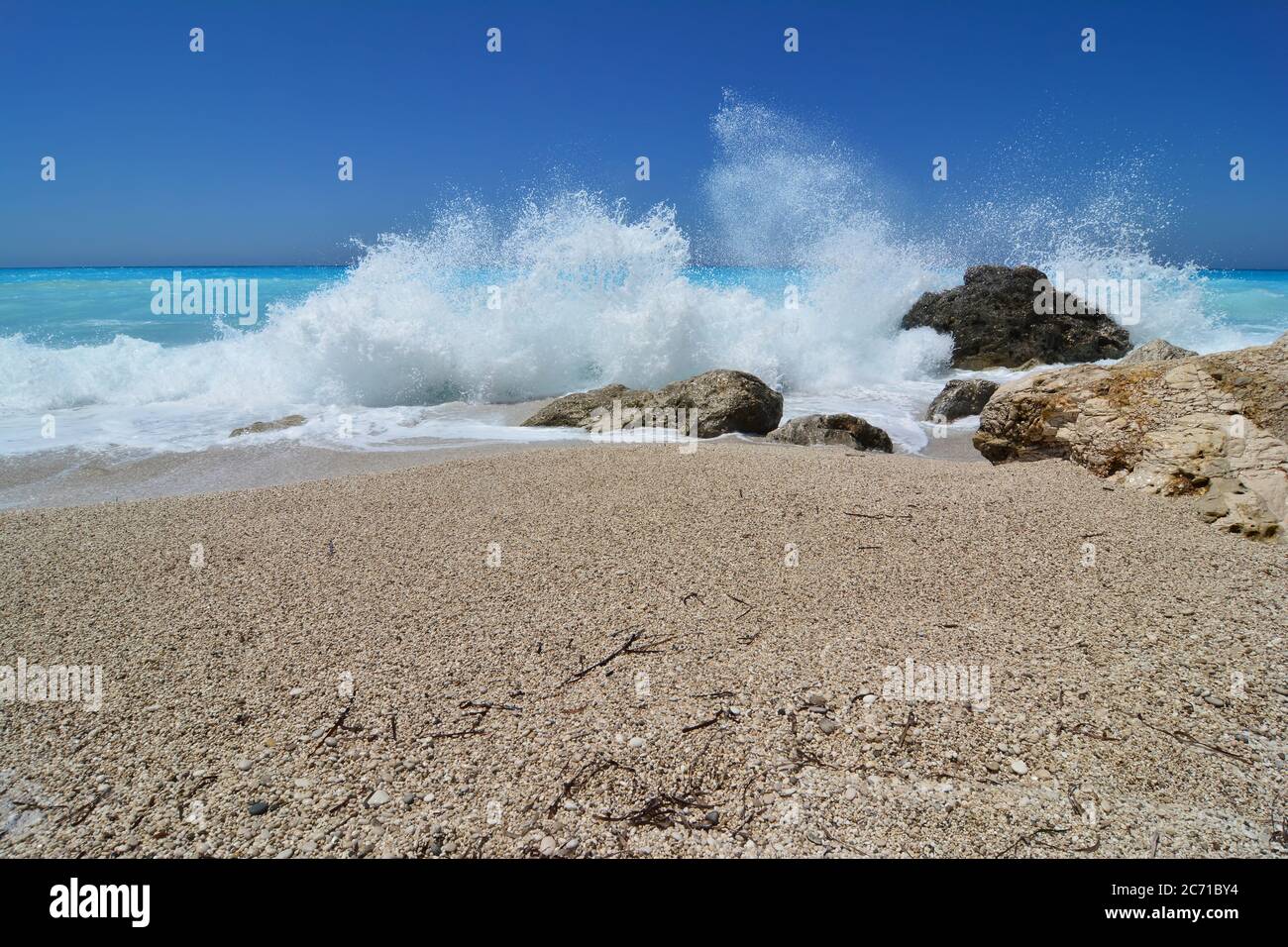 Clear sky and beach after storm, big waves splashing over rocks ...