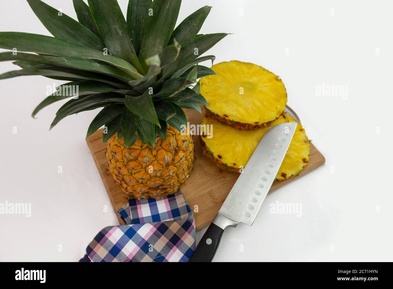 shot of three quarters of a pineapple with slices, knife and napkin on ...