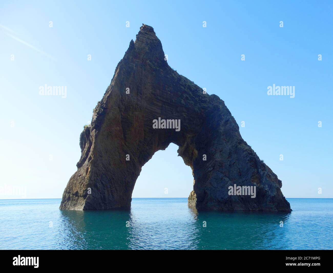 A triangular rock with an arch in the middle protrudes from the sea ...