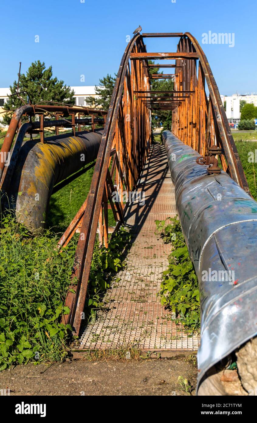 Old rusty iron bridge over the river with a steam pipeline. Heat supply ...