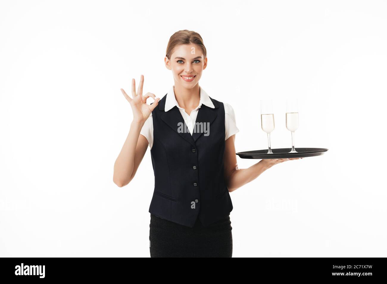 Young smiling waitress in uniform holding tray with glasses happily ...