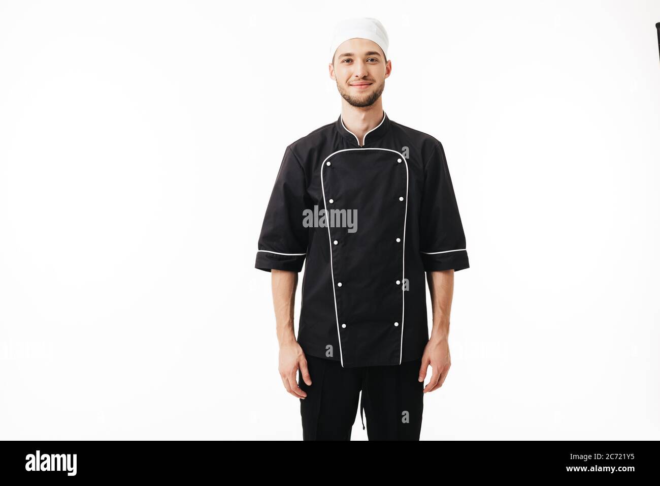 Young man chef in black uniform and white cap dreamily looking in ...