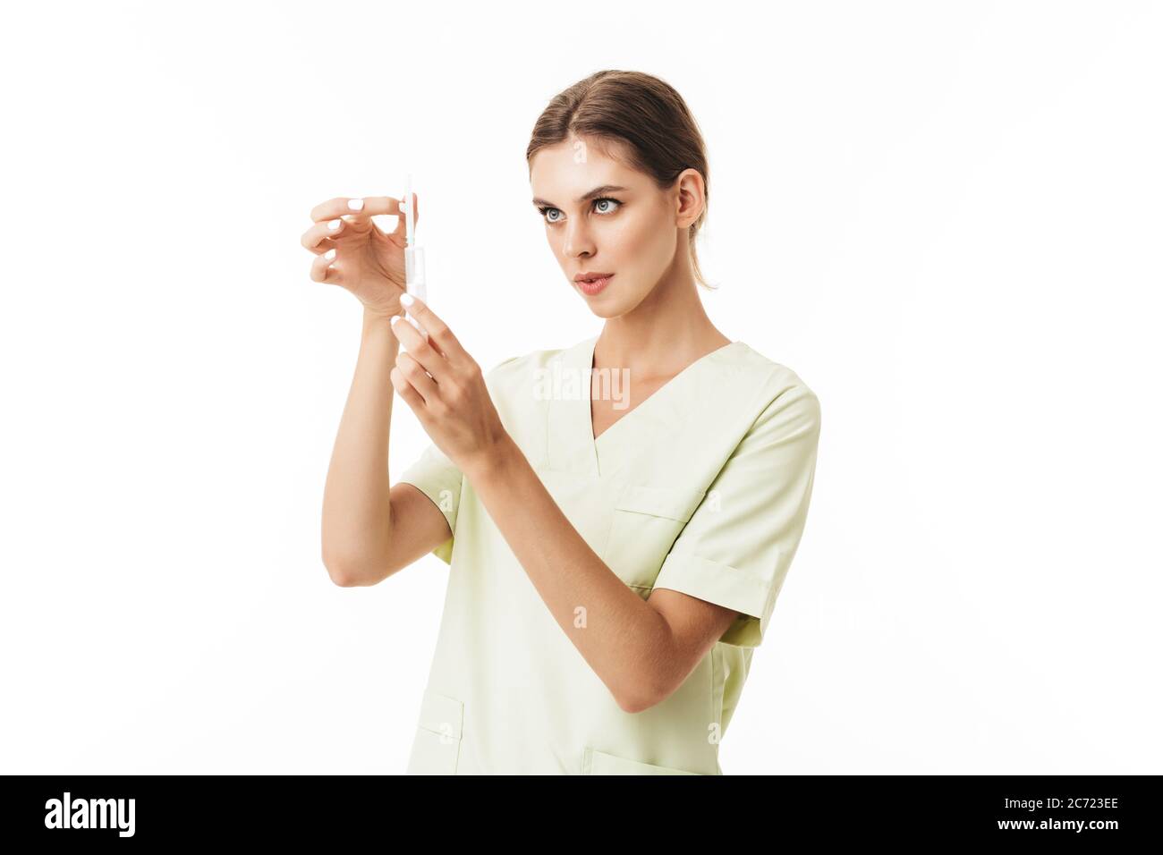 Young pretty nurse in uniform thoughtfully holding syringe in hands ...