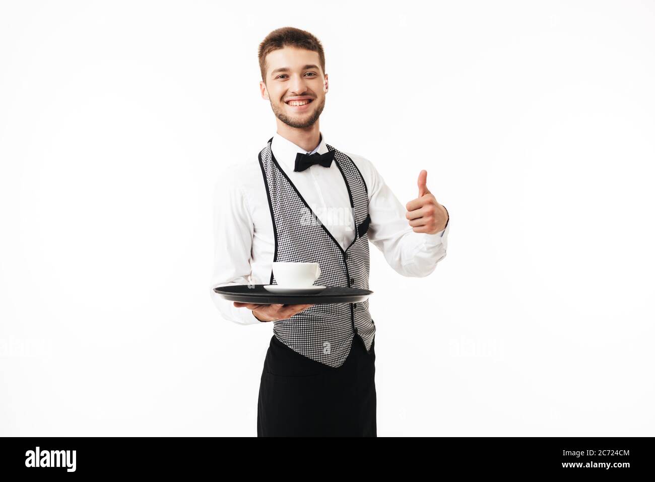 Young smiling waiter in uniform holding tray with cup of coffee in hand ...