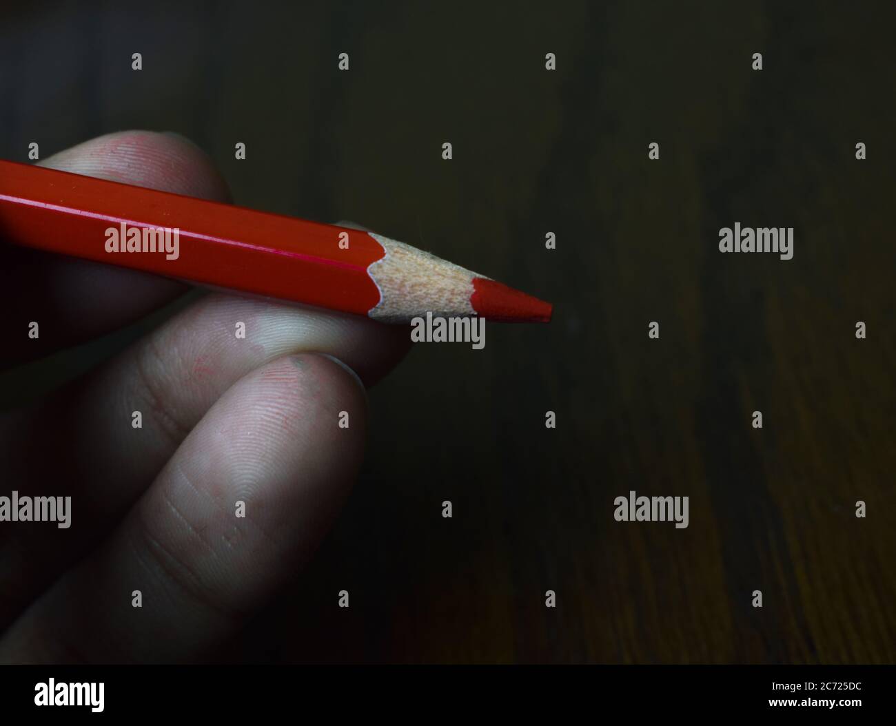 Person holding a red color wood pencil crayon with his hand on a brown ...