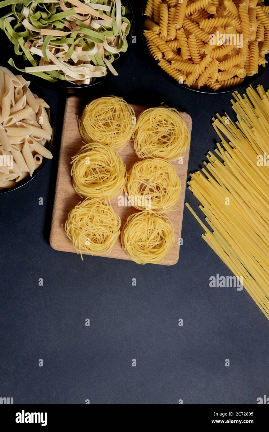 Different types of dry pasta on the plate and in bowls on black ...