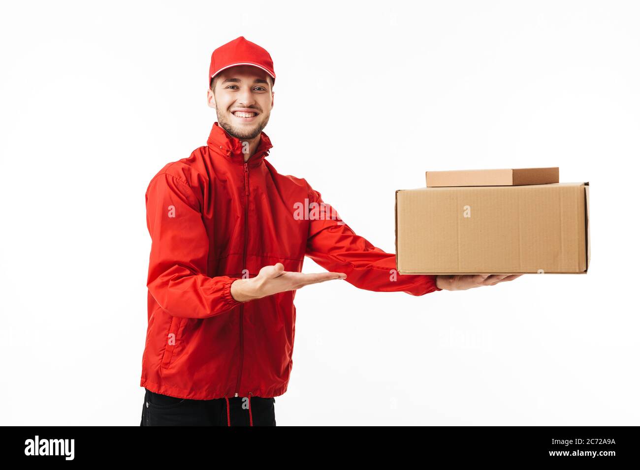 Young joyful delivery man in red cap and jacket happily looking in ...