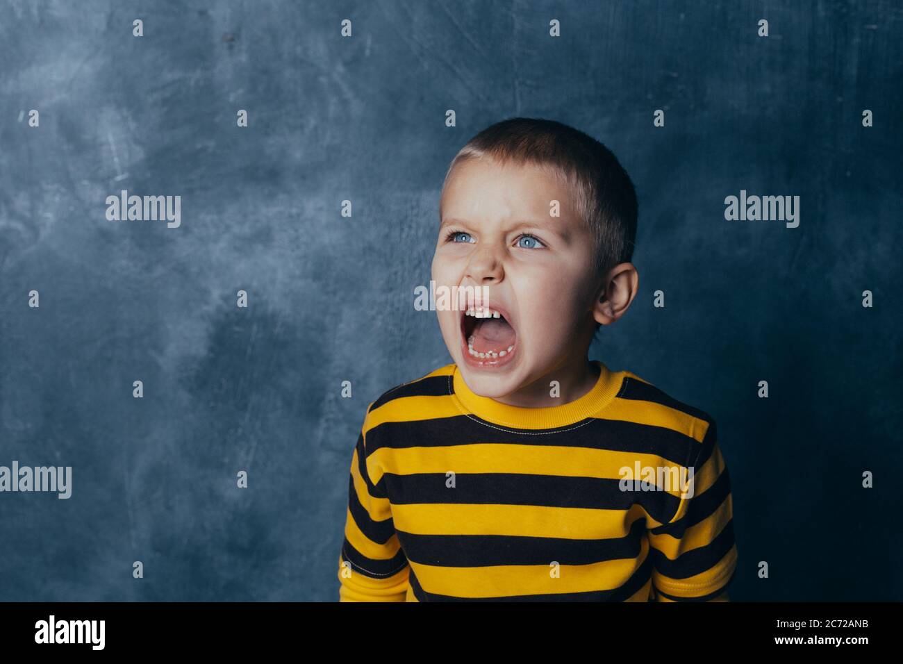 A little boy poses in front of a gray-blue concrete wall. Portrait of a ...