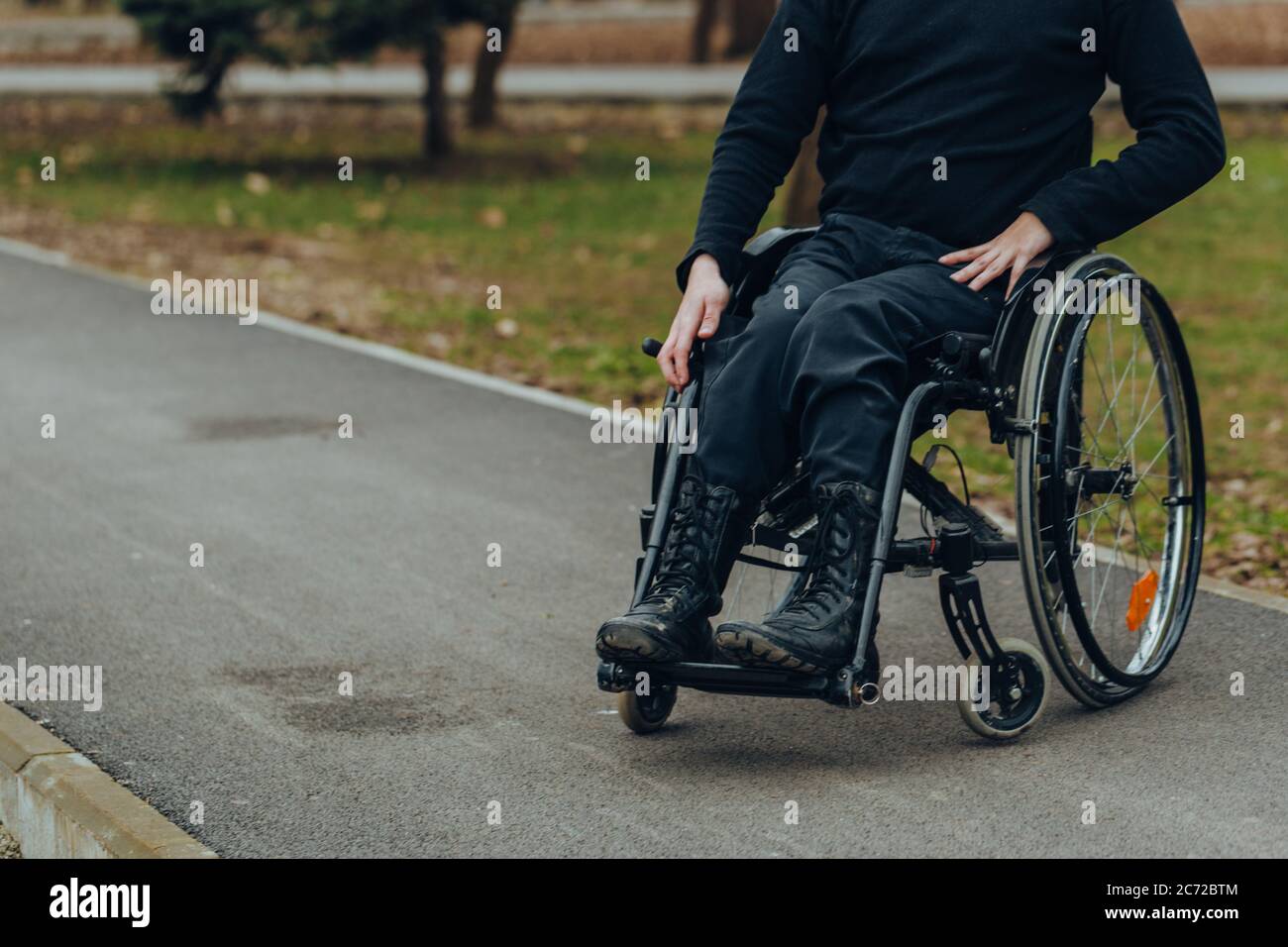 Close-up of male hand on wheel of wheelchair during walk in park. He ...