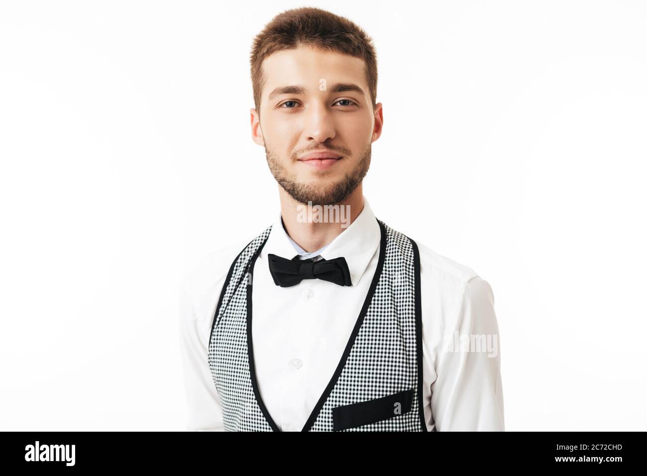 Portrait of young smiling waiter with beard in bow tie dreamily looking ...