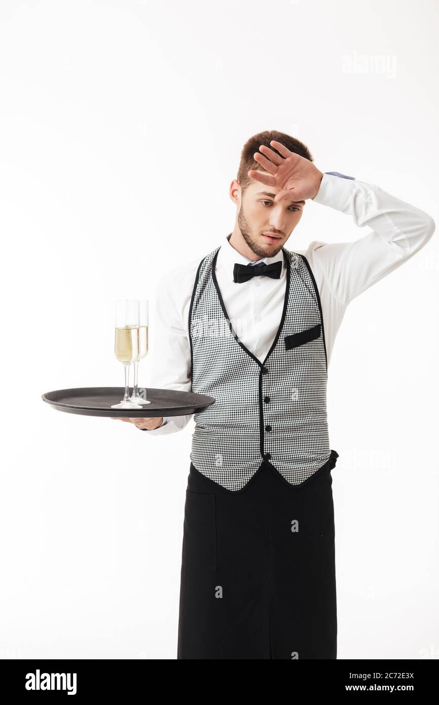 Young tired waiter in uniform holding tray with glasses of champagne ...