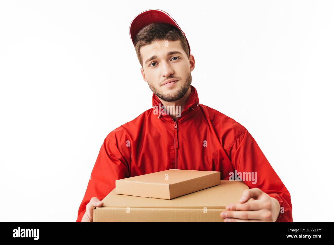 Young tired delivery man in red cap and jacket holding boxes in hands ...