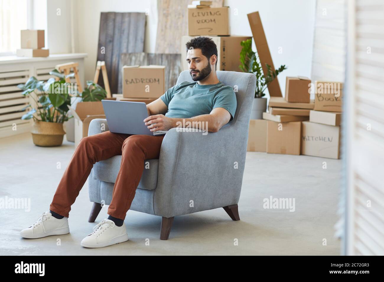 Young bearded man sitting on armchair and using laptop computer he ...