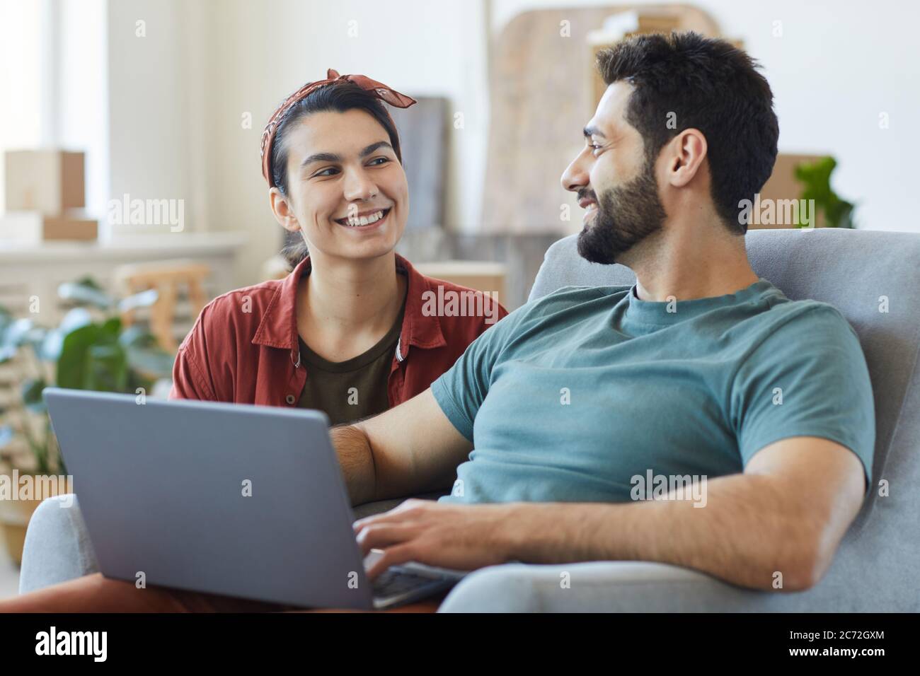 Young Happy Couple Sitting On Sofa Talking To Each Other And Using