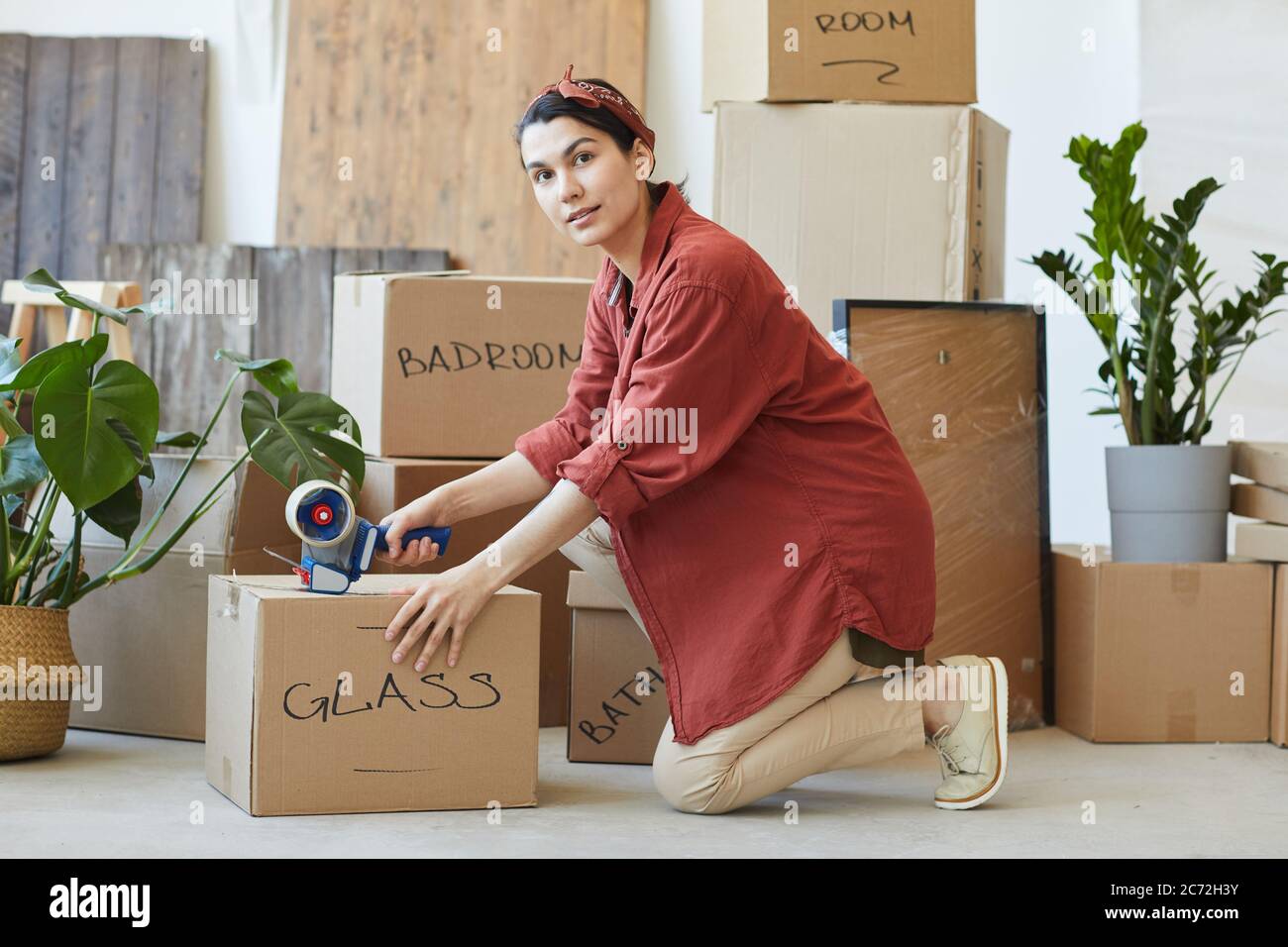 Portrait of young woman packing things in boxes and using adhesive tape ...