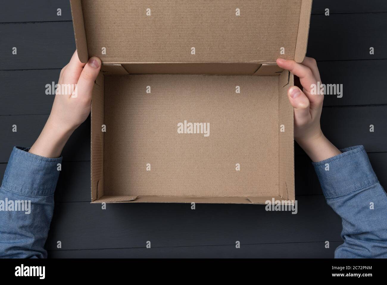 Children's hands holding an open cardboard box. Empty box, black ...