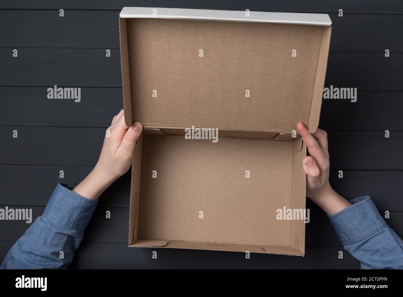 Children's hands holding an open cardboard box. Empty box, black ...