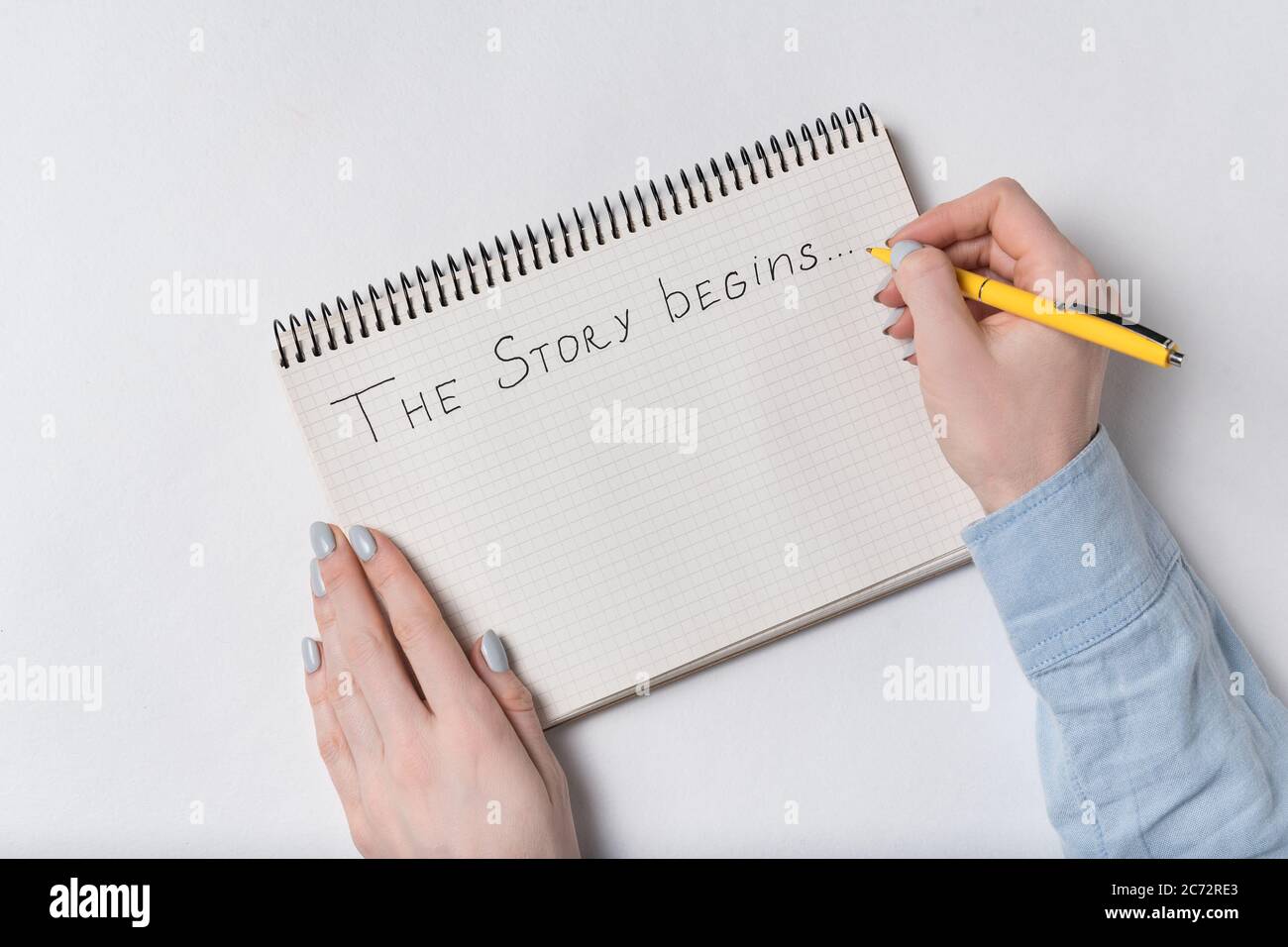 THE STORY BEGINS text in copybook. Female hands writing note in Notepad ...