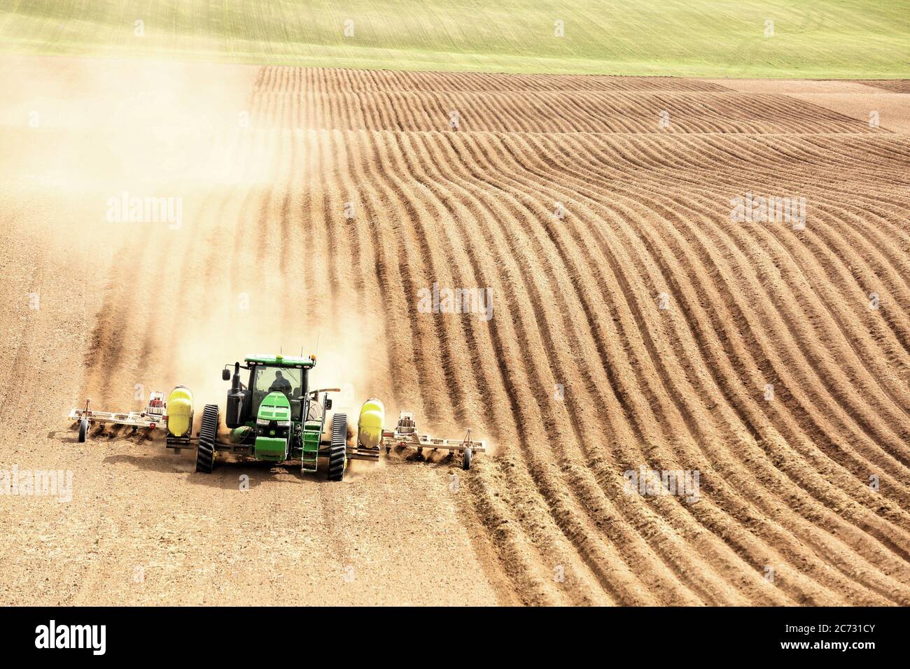 A tractor in a farm field, pulling a plowing and cultivation implement ...