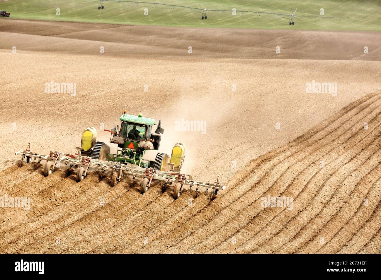 A tractor in a farm field, pulling a plowing and cultivation implement ...