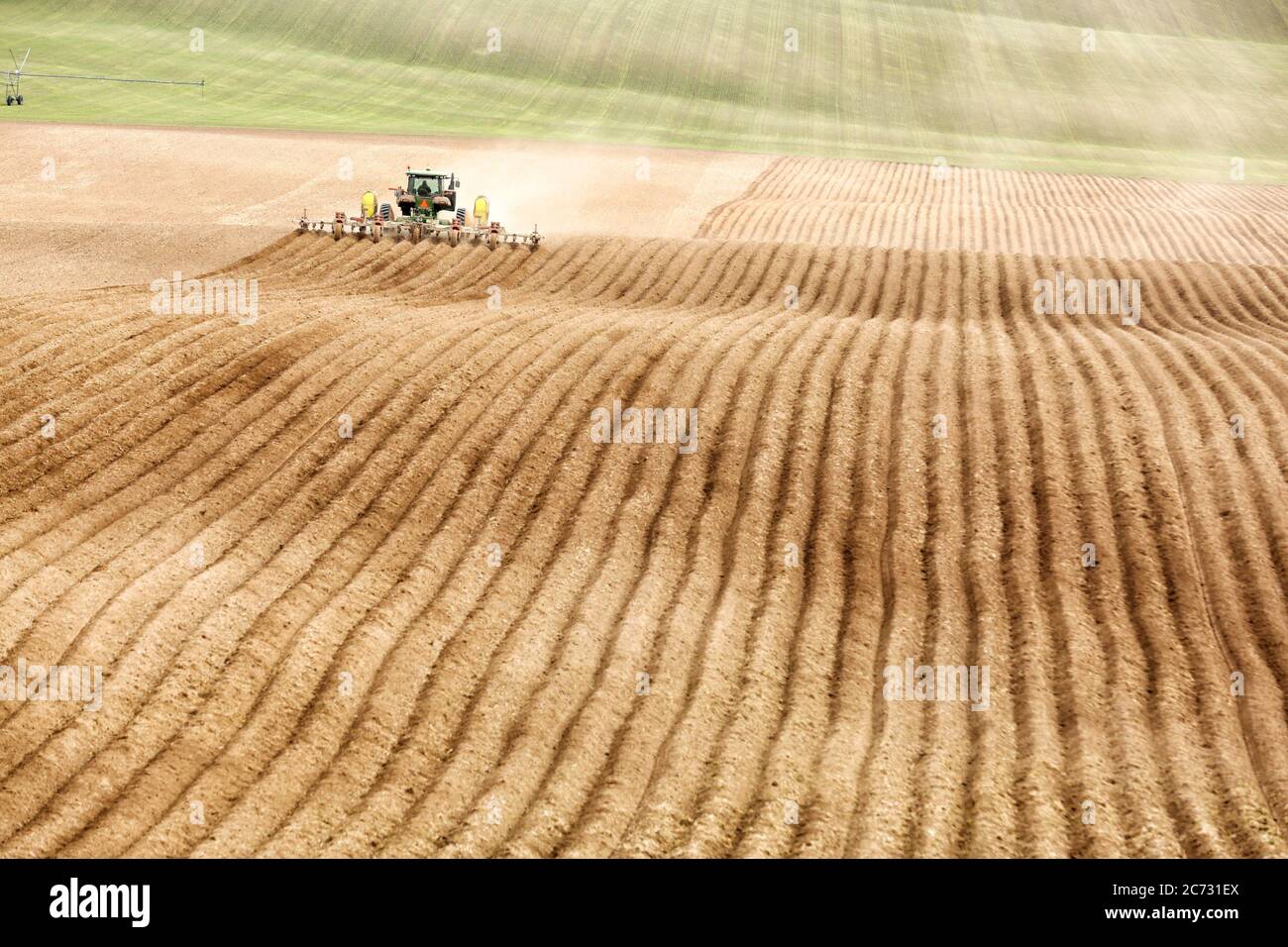 A tractor in a farm field, pulling a plowing and cultivation implement ...