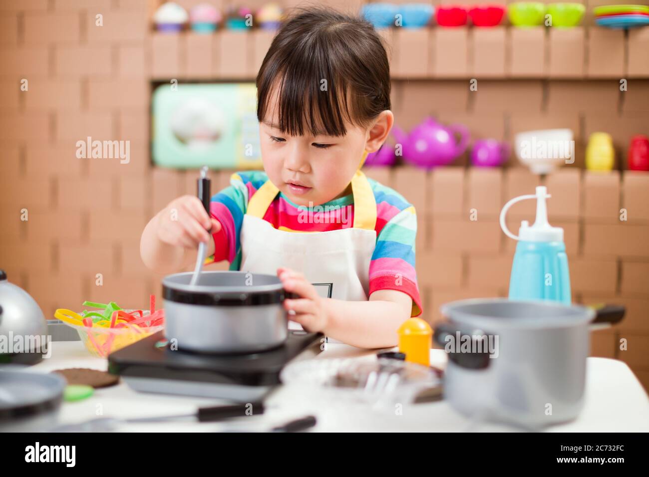 toddler girl pretend play food preparing role against cardboard blocks ...