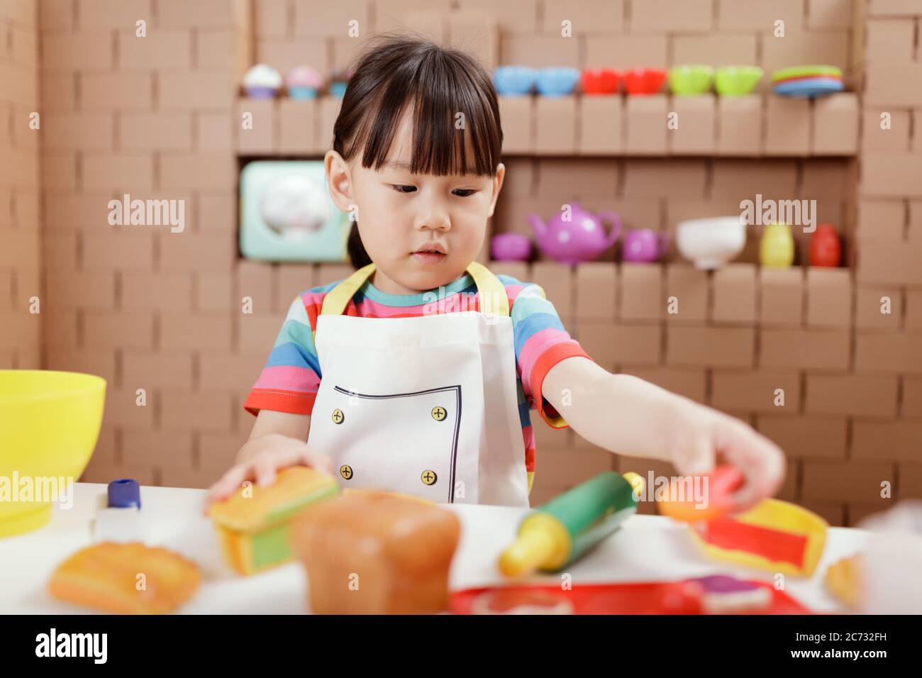 toddler girl pretend play food preparing role against cardboard blocks ...