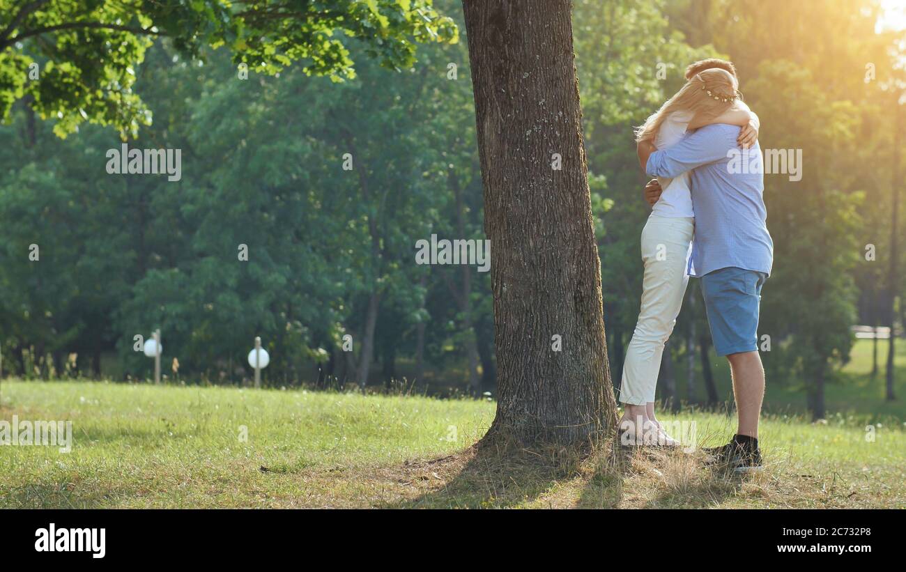 A young man and woman are standing under a tree in a park and hugging ...