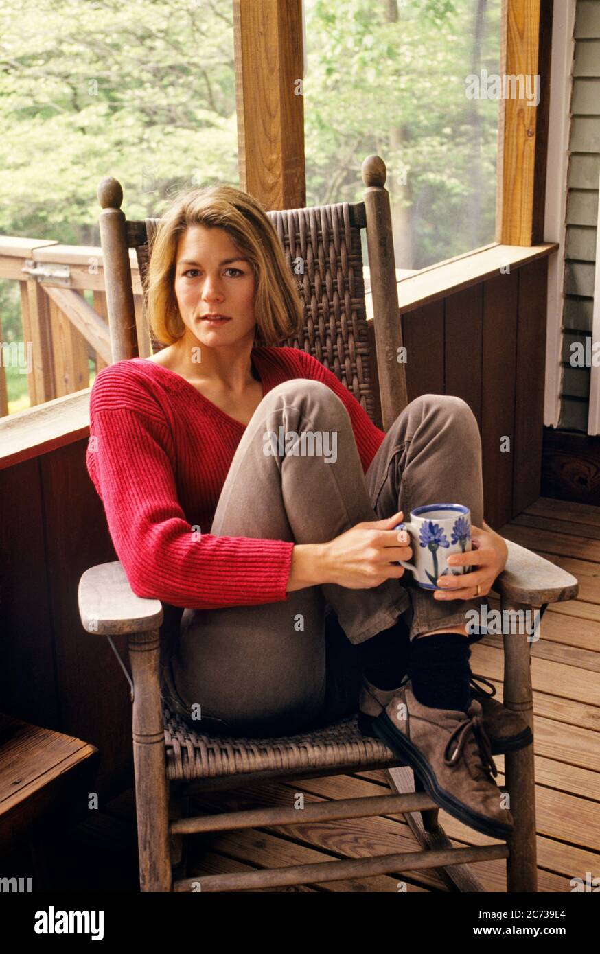 1990s WOMAN RELAXING ON SCREENED PORCH SITTING IN ROCKING CHAIR HOLDING ...