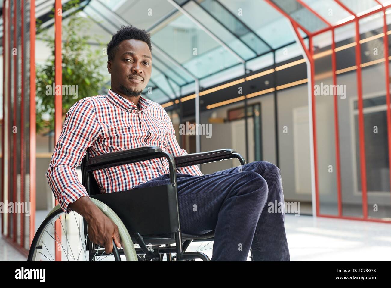 Portrait of African young disabled man sitting in wheelchair at office ...