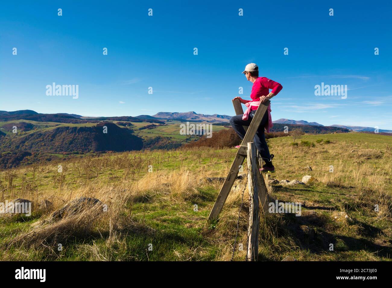 Walker walker climbing over stile. Sancy massif at back, Auvergne ...