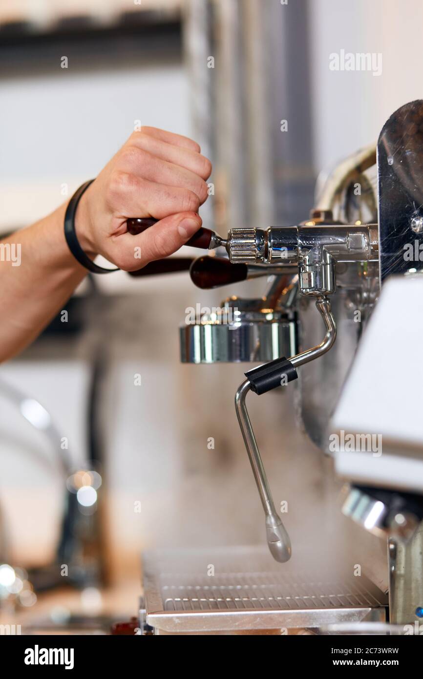 Strong hand of young barista turns handle of coffee machine with effort ...