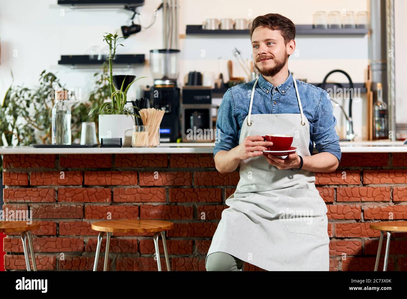 Pleasant romantic male barista looks away with dreamy feelings, stands ...