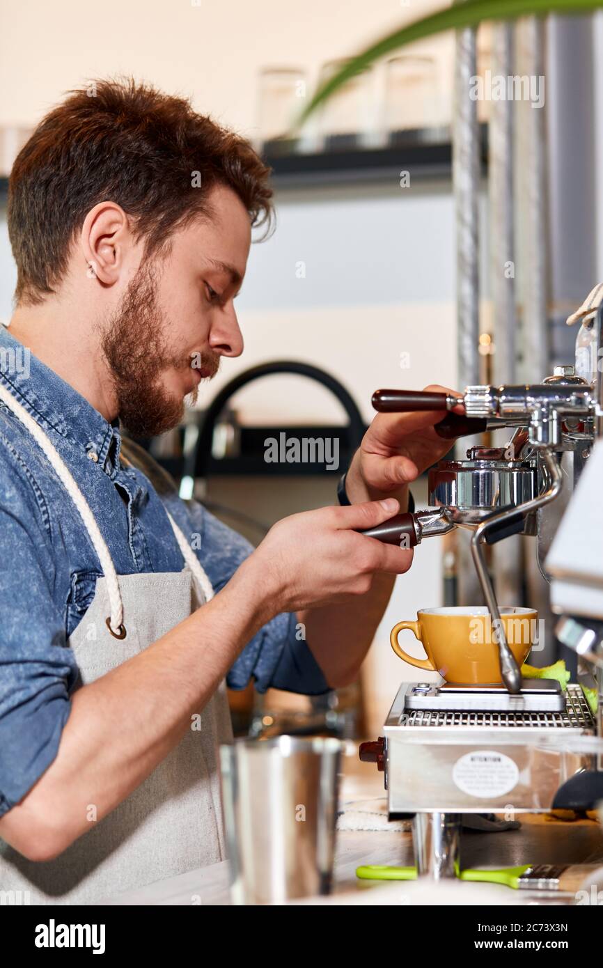 Professional male barista, wears jeans shirt and neat apron, stands by ...
