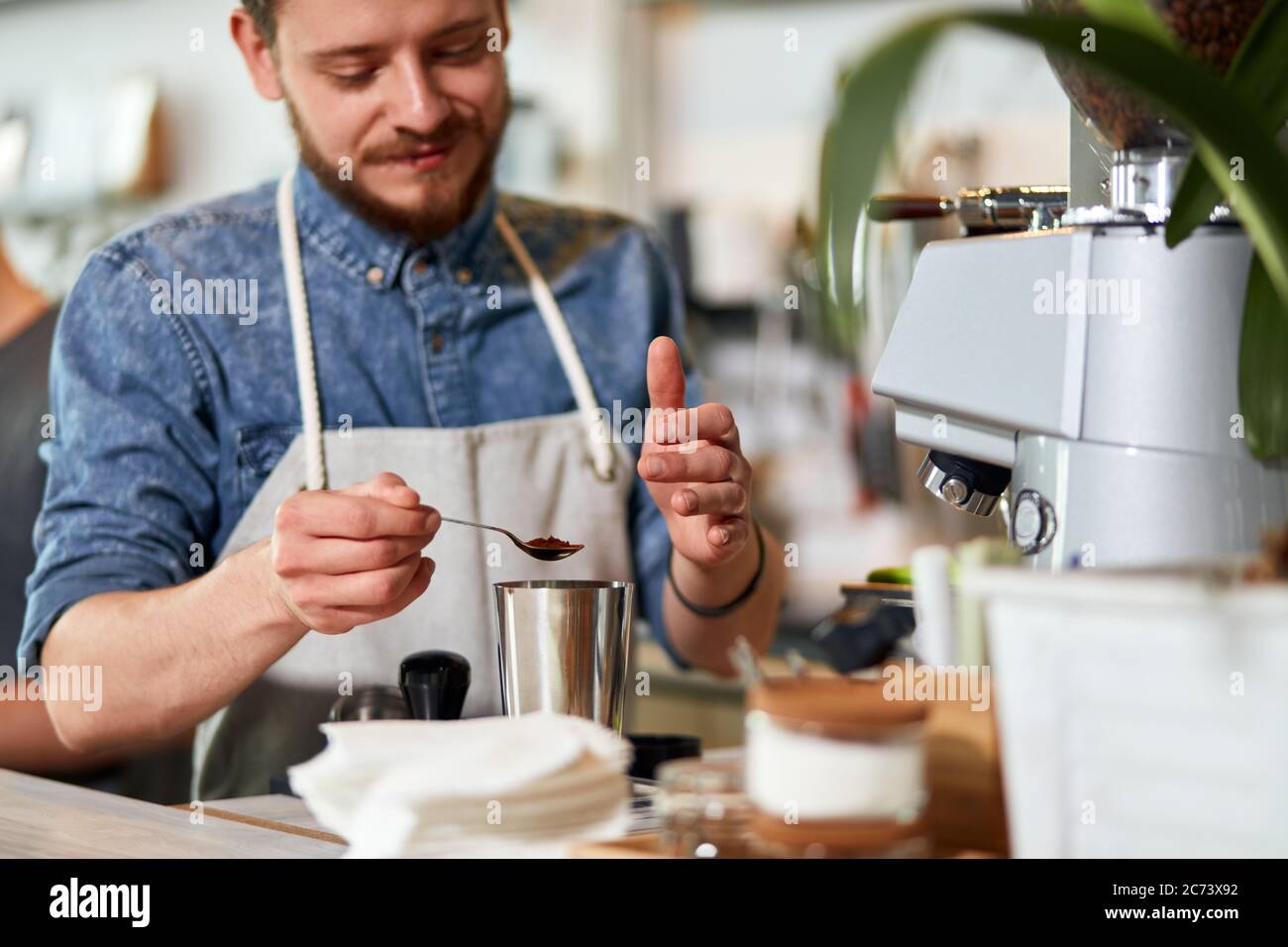 Handsome peaceful male barista stands in apron behind counter, keeps ...