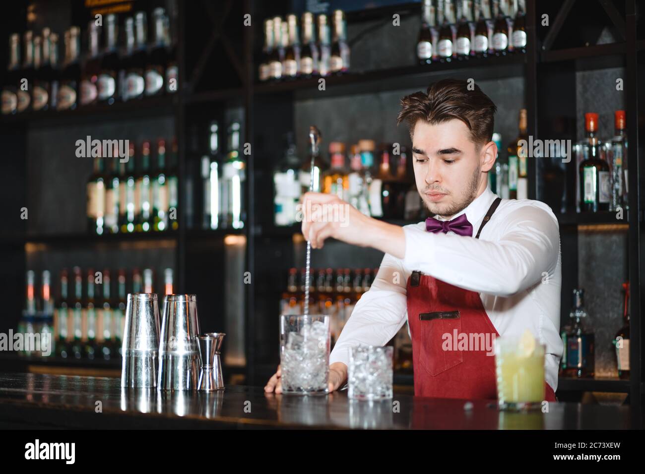 Barman mixing cocktail ingredients with a long spoon in high glass ...