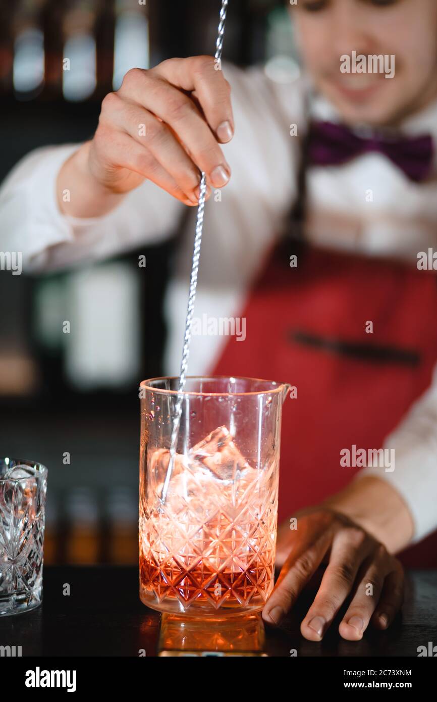 Bartender using long metal spoon to mix ice cubes with drink in a glass ...