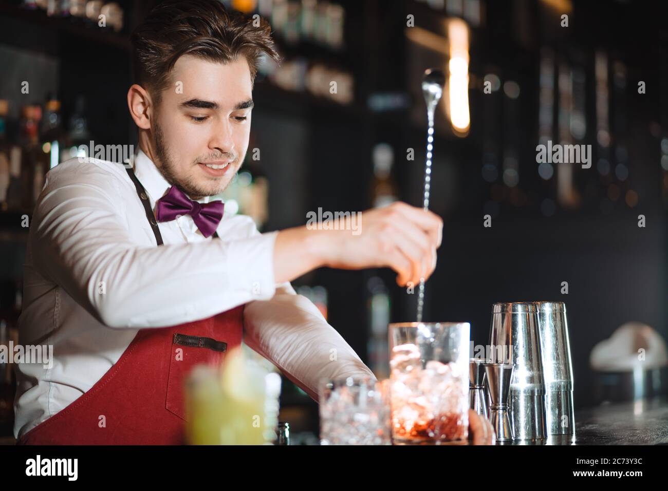 Barman holding a long spoon and glass filled with ice cubes and red ...