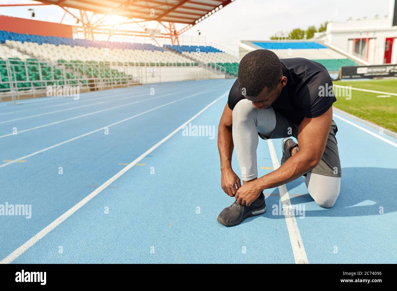 Sportsman ties his trainers, sitting on the running track, preparing ...