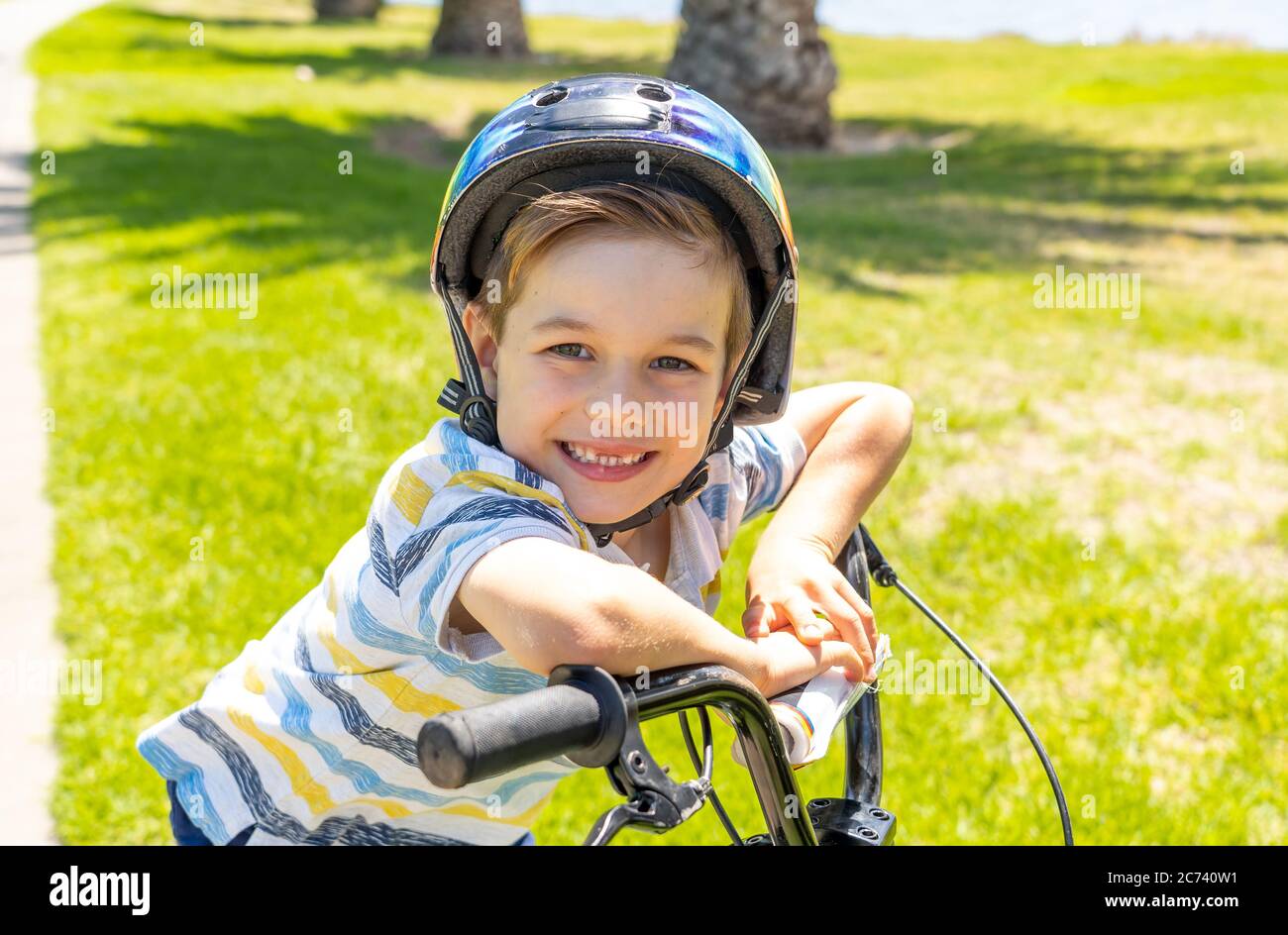 Cute cheerful boy with helmet on his new bike by the lake at the park ...