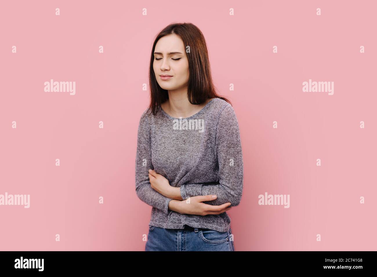 Portrait of sad young girl wincing in pain and clutching belly beacuse ...