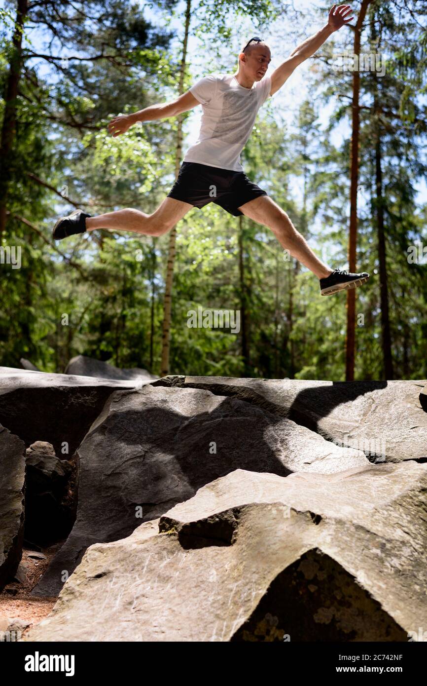 Young man jumps on a rock in a coniferous forest. Active extreme ...