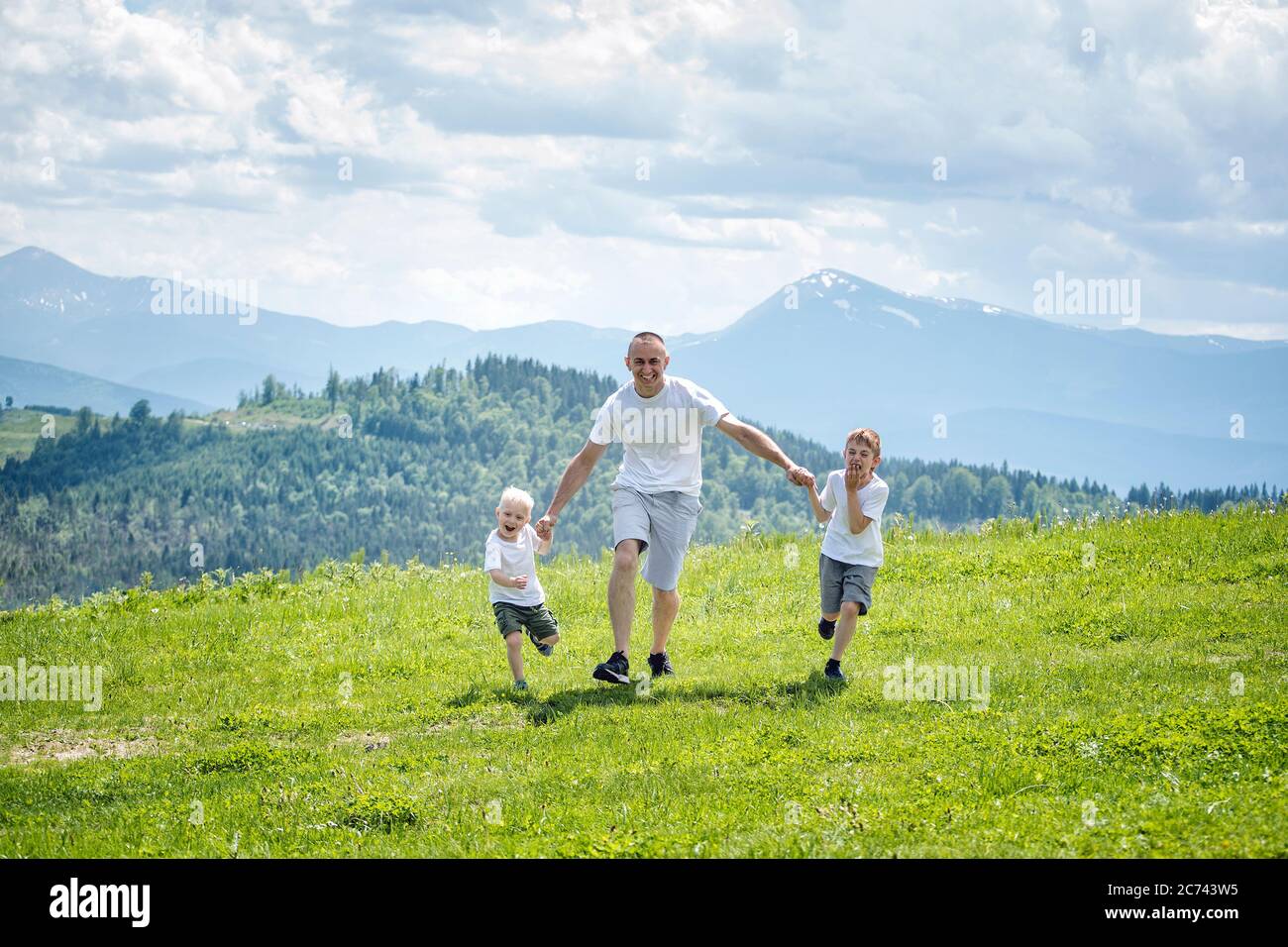 Father and two young sons running on the green field holding hands on ...