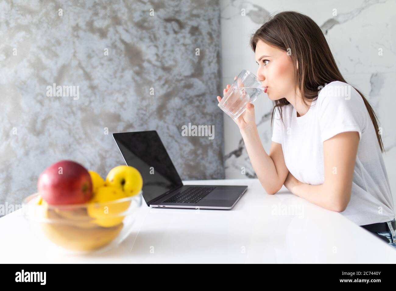 Woman drinking from water glass while typing at her laptop Stock Photo ...