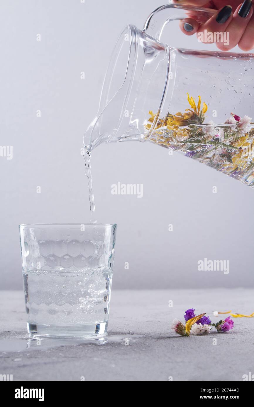 Pouring clean water with flowers into glass cup Stock Photo - Alamy
