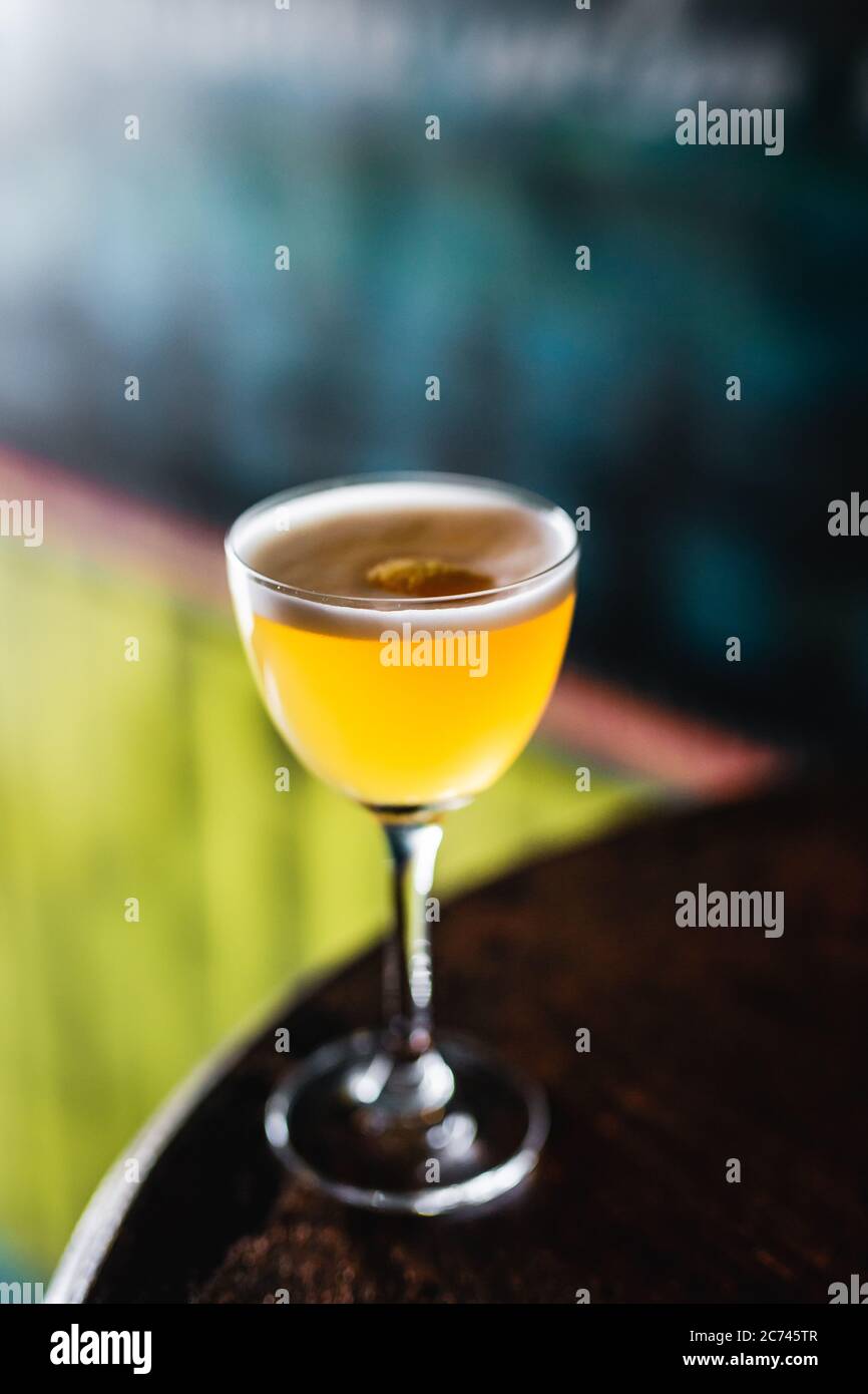 A sour cocktail in a nick and nora glass with orange peel garnish on ...