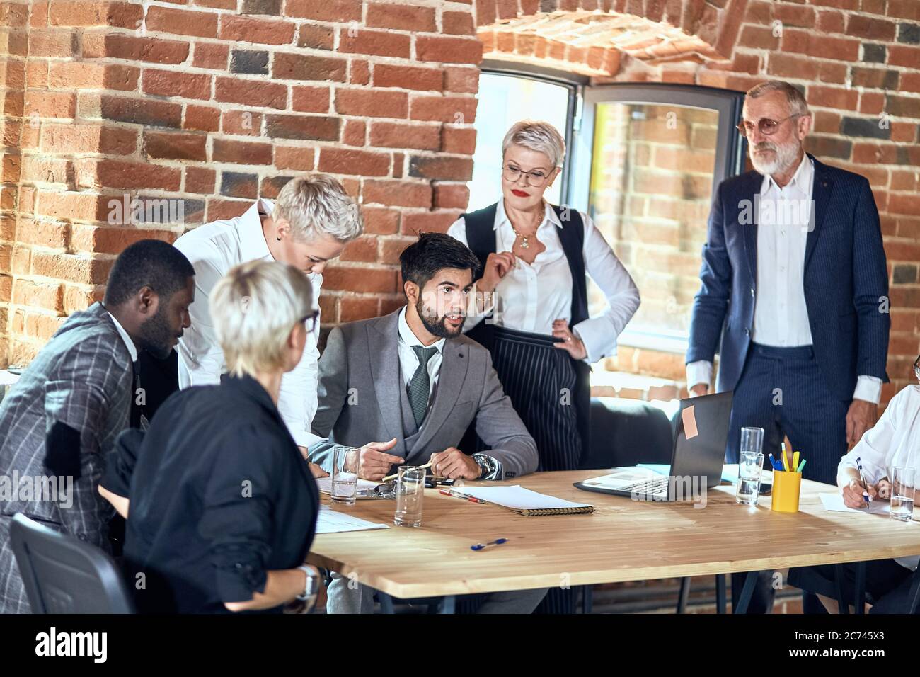 Group of businessmen around table in office brick wall. Cacausian adult ...