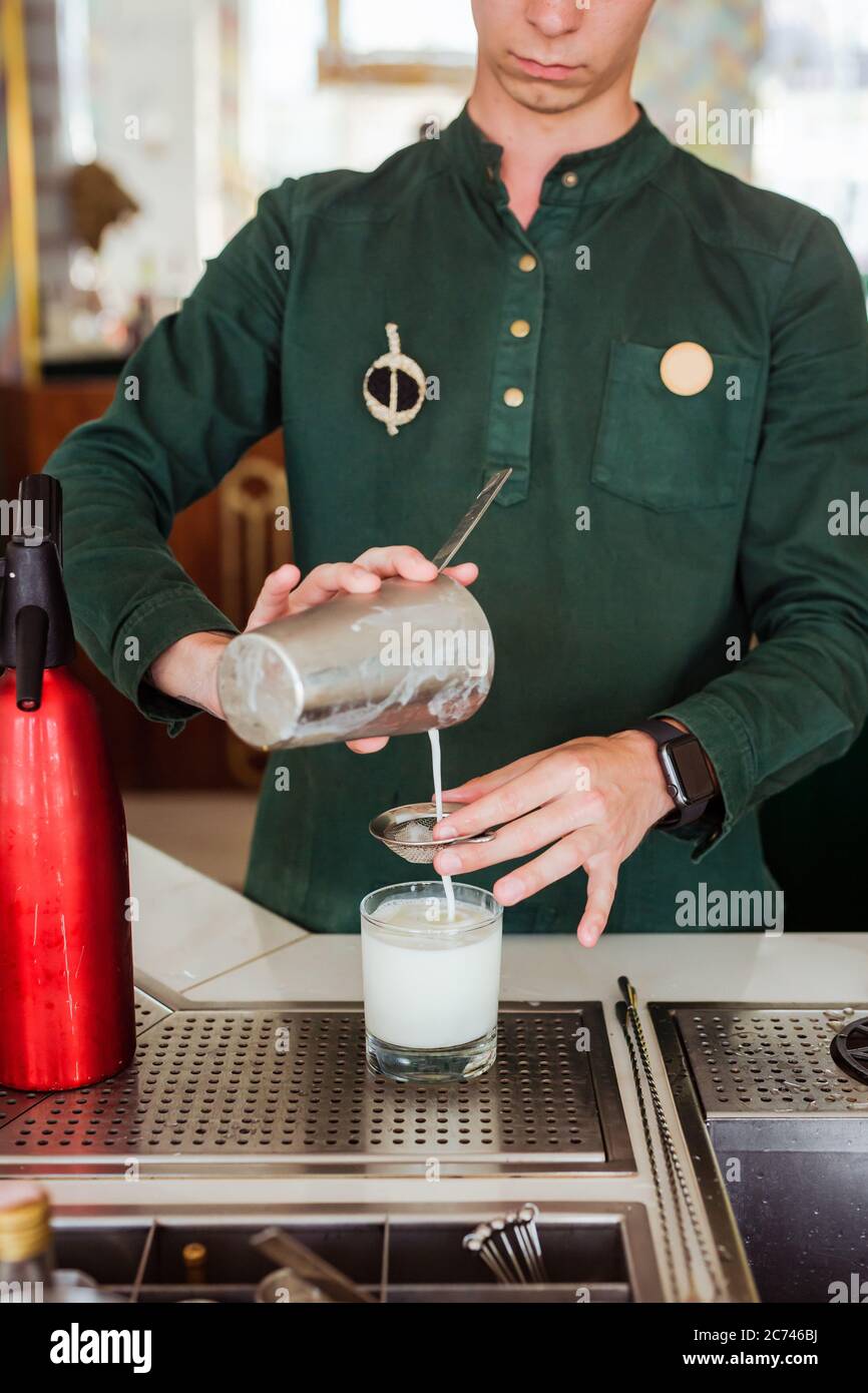 Bartender making a cocktail at the bar: pouring a drink from a shaker ...